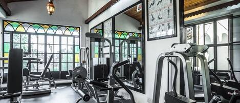 Uma academia com equipamentos de exercício, janelas amplas e vigas de madeira no teto.