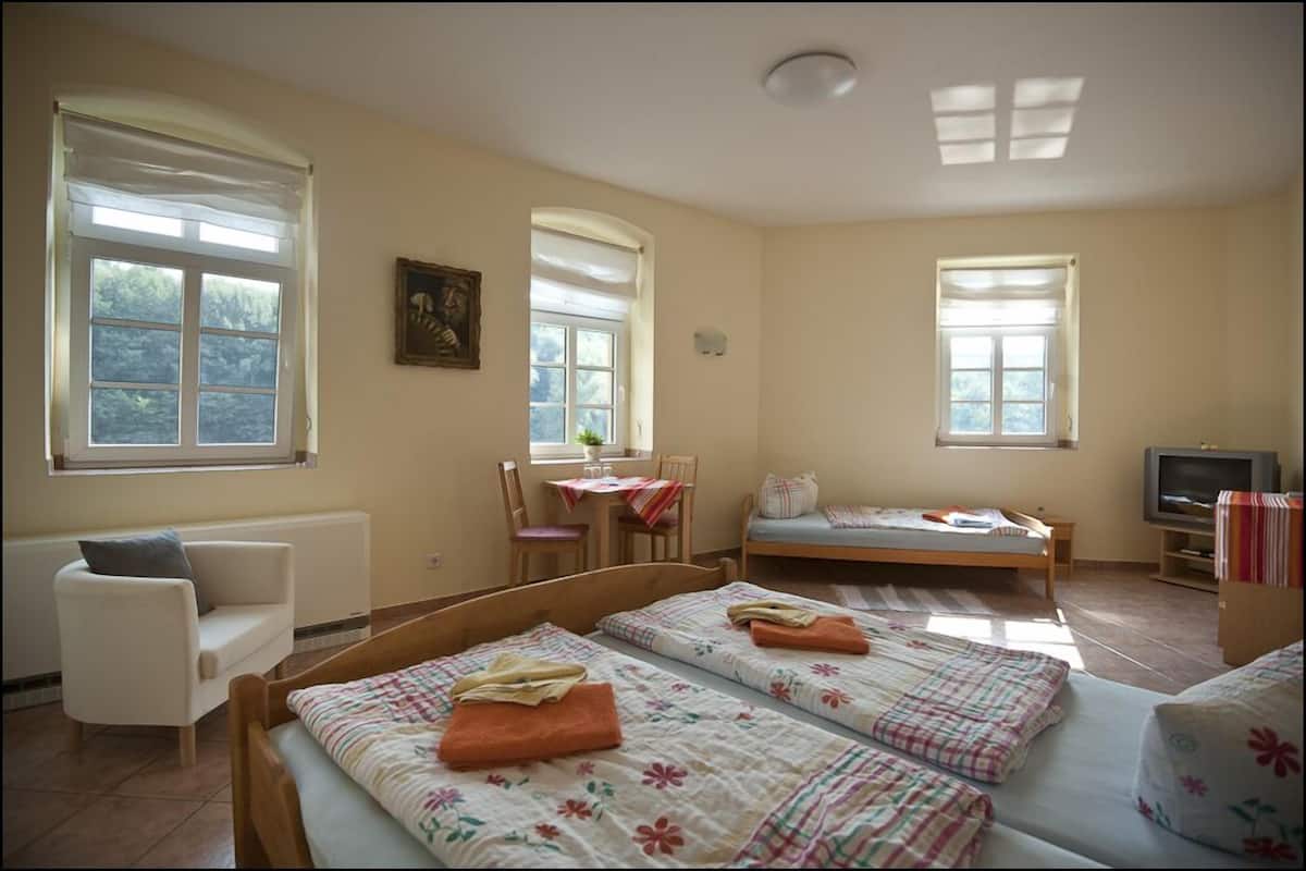 Quarto com duas camas, um sofá, uma TV e um espaço de refeições com mesa e cadeiras.