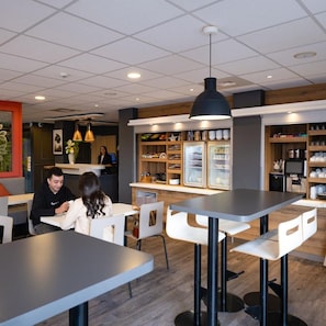 Interior moderno de café, com mesas, cadeiras e balcão com alimentos expostos.
