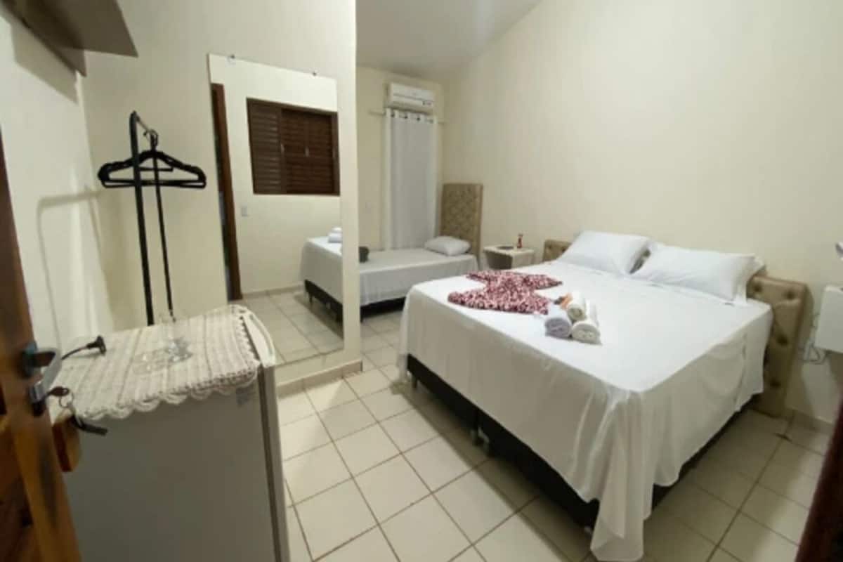 Quarto de hotel com cama, mesa de cabeceira, cabideiro e área de chuveiro.