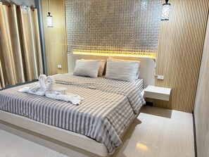 Quarto de hotel com cama, mesa de cabeceira, luminária na parede e painel decorativo.