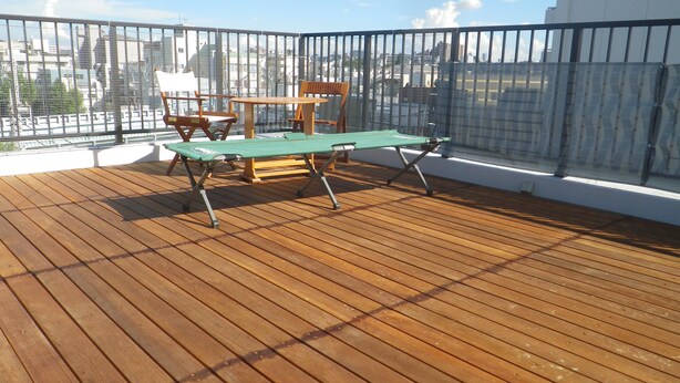 Um deck de madeira com mesa e cadeiras, cercado por uma grade de metal.