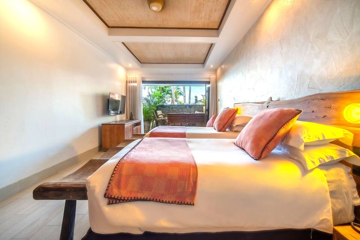 Quarto de hotel moderno com uma cama grande, cabeceira de madeira e vista para o exterior.