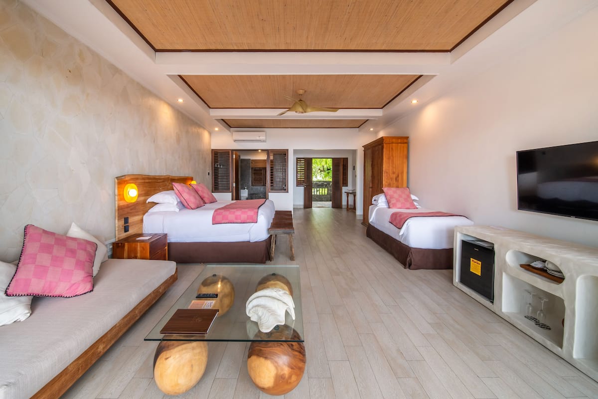 Quarto de hotel com duas camas, um sofá, uma mesa de centro de vidro, uma televisão e um minibar.