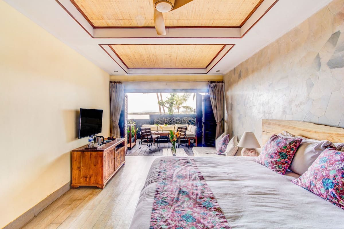 Quarto com cama, televisão, armário de madeira e varanda com mesa e cadeiras.