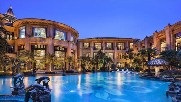 Um hotel com uma piscina grande e central, várias varandas e uma fachada bem iluminada.