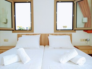 Cama de casal com lençóis brancos, duas janelas e cabeceira de madeira.