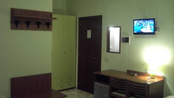 Um quarto pequeno e com pouca luz, com uma cama, uma escrivaninha, uma cadeira, uma televisão e um guarda-roupa.