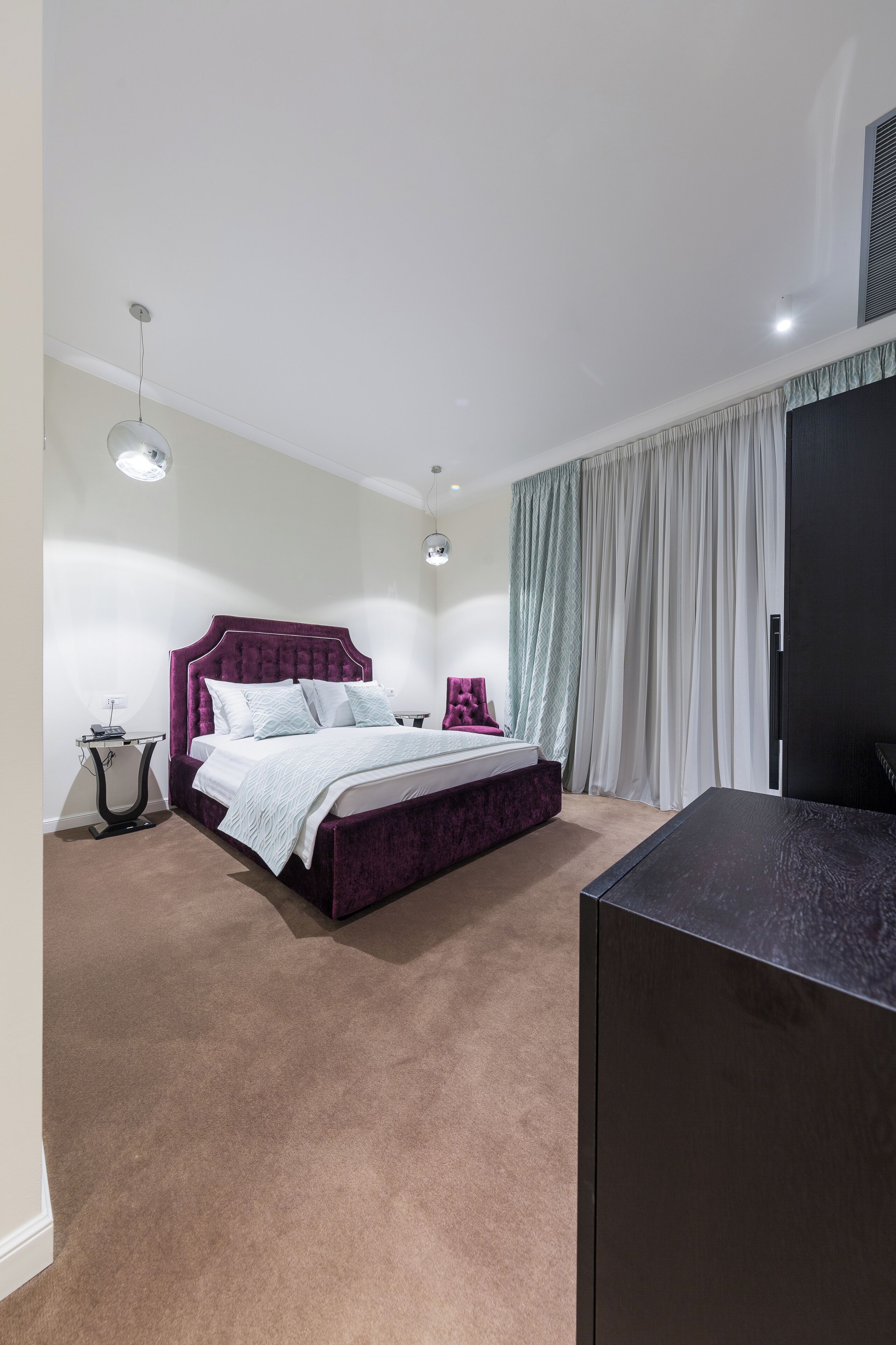 Quarto moderno com uma cama grande, mesa de cabeceira, televisão e cortina.