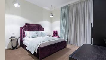 Quarto moderno com uma cama grande, mesa de cabeceira, televisão e cortina.