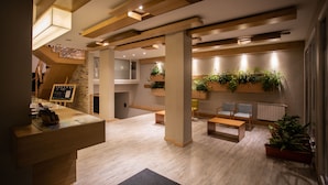Uma área de recepção moderna com vigas de madeira, balcão de atendimento, assentos e plantas em vasos.