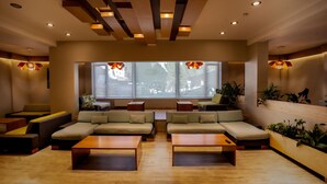 Espaço lounge moderno com sofás, mesas e plantas em vasos.