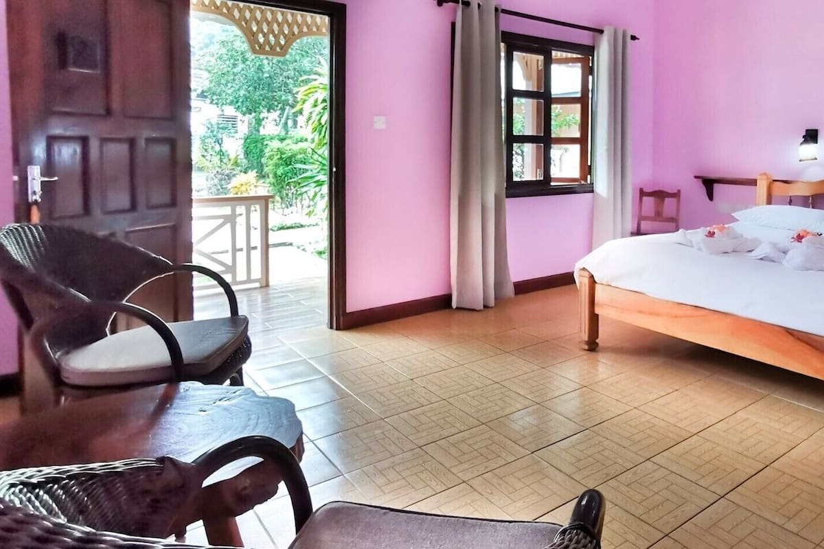 Quarto com cama, cadeira, mesa e janela com cortinas.