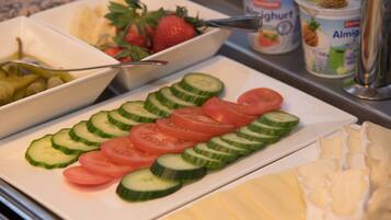 Buffet com pepinos fatiados, tomates e uma tigela de morangos.