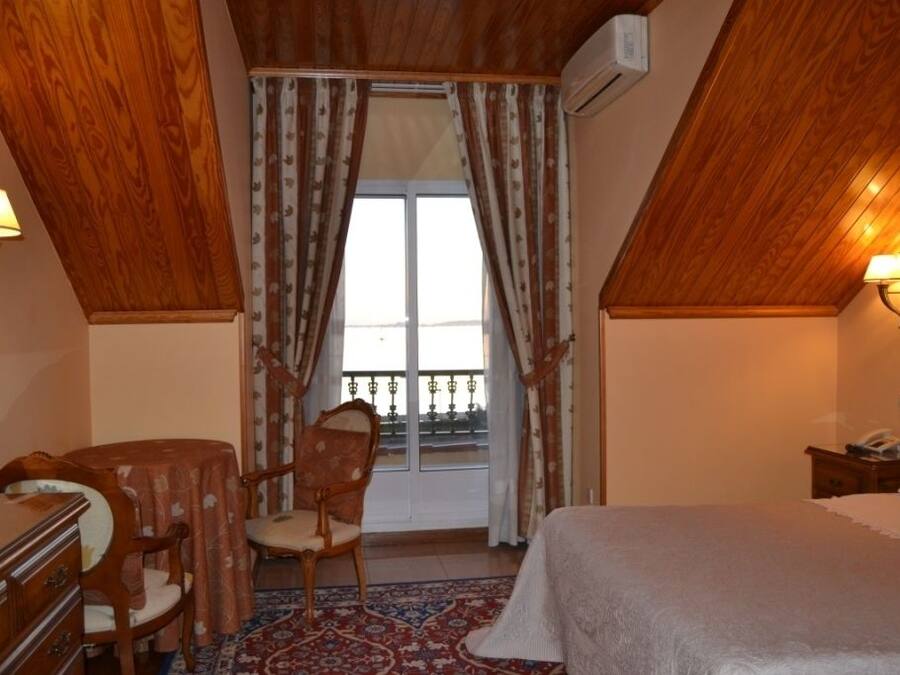 Um quarto com uma cama, uma cadeira, uma mesa e uma janela com cortinas.