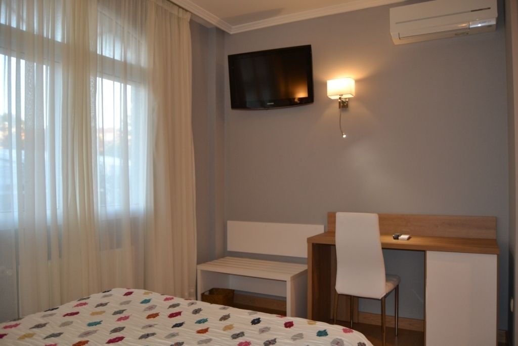 Quarto de hotel com cama, escrivaninha, cadeira, televisão e ar condicionado fixado na parede.