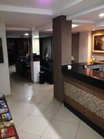 Um hall de hotel com balcão de recepção, área de estar com sofás e piso ladrilhado.