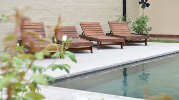 Área ao redor da piscina com espreguiçadeiras de madeira e uma pequena planta em vaso.