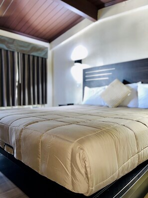Uma cama com cabeceira acolchoada, uma luminária de cabeceira e vista para uma janela com persianas.