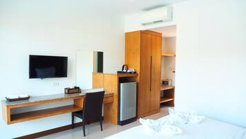 Quarto de hotel com cama, escrivaninha, cadeira, televisão, frigorífico e guarda-roupa.