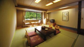 Um quarto japonês tradicional com tatames, uma mesa de madeira baixa e uma televisão.