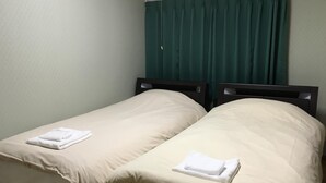 Quarto com duas camas de solteiro, cada uma com um cobertor branco e uma toalha dobrada.