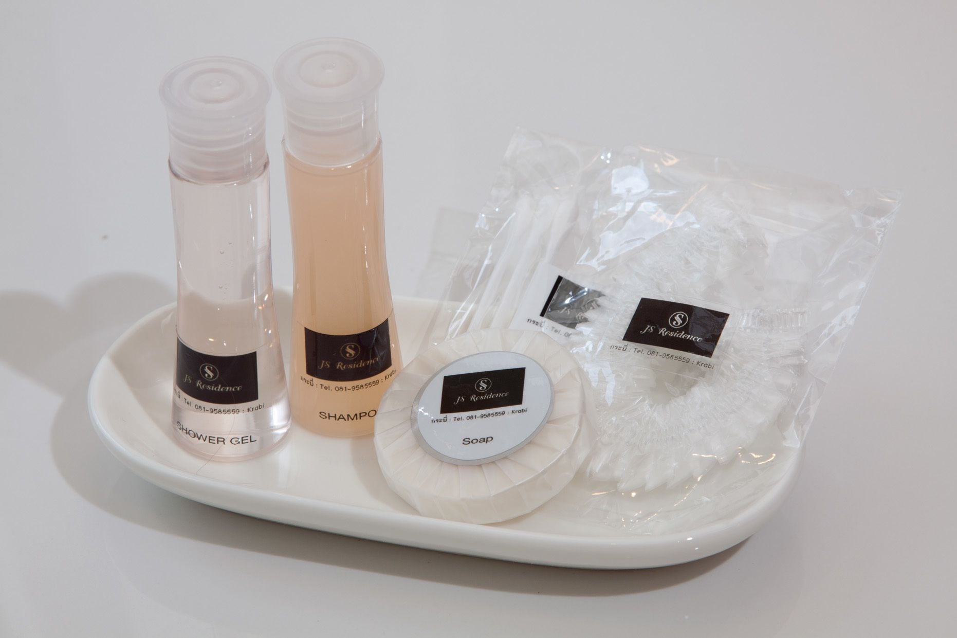 Uma bandeja com duas embalagens de gel de banho, uma embalagem de shampoo e um sabonete, todos identificados com 'JS Residence'.