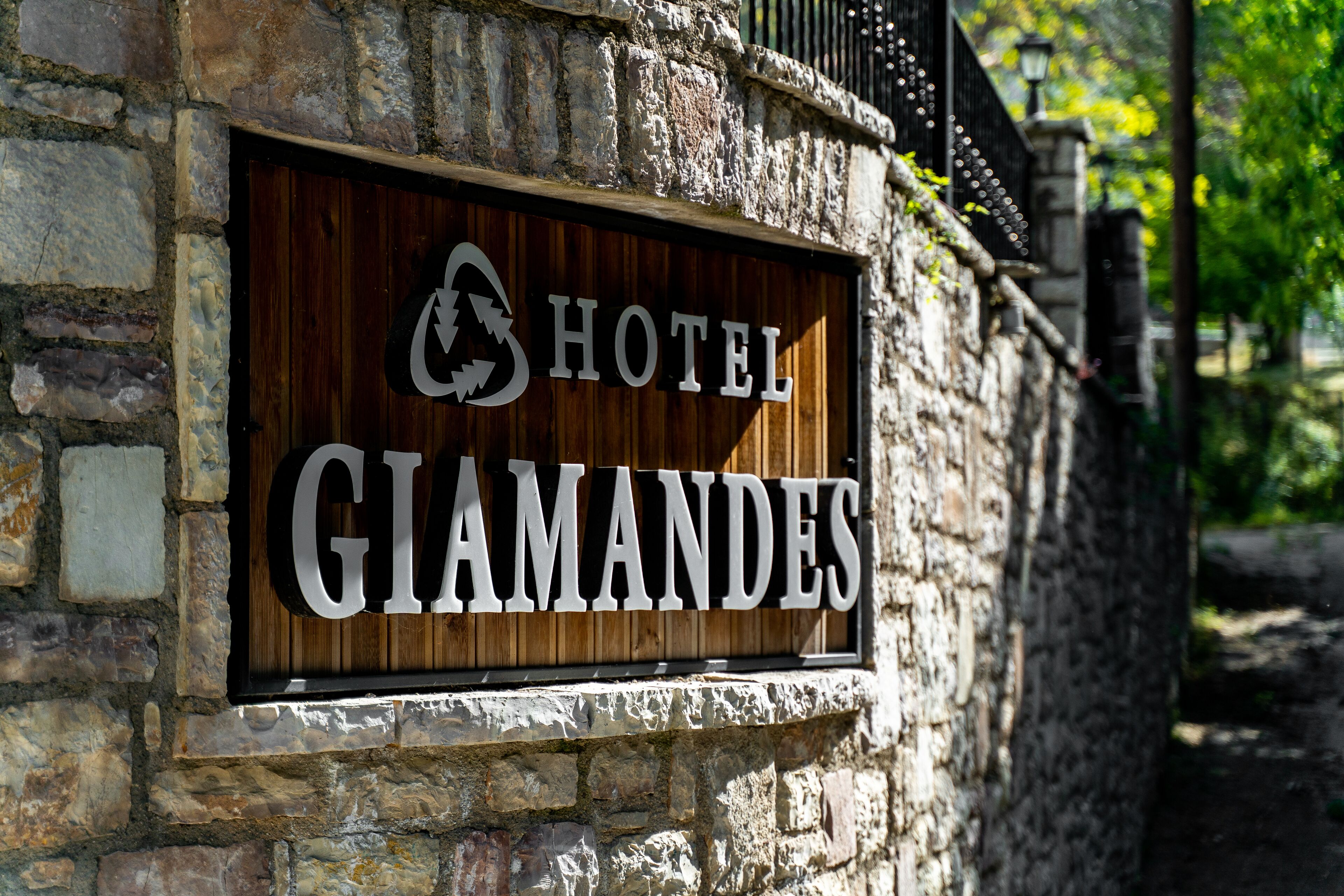 Uma placa de madeira com as palavras 'HOTEL GIAMANDES' e um ícone de montanha.