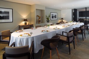 Mesa de jantar comprida com cadeiras, rodeada por paredes com quadros e objetos decorativos.