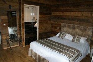 Quarto de cabana de madeira com uma cama, uma cadeira e um banheiro visível através de uma porta aberta.