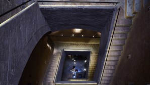 Uma escadaria estreita com paredes de pedra e um pequeno espaço no final, com uma mesa e uma cadeira.