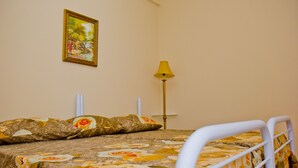 Um quarto com cama, luminária de cabeceira, quadro na parede e janela.