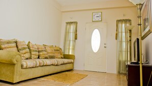 Uma sala de estar com sofá, cortinas, relógio e luminária.