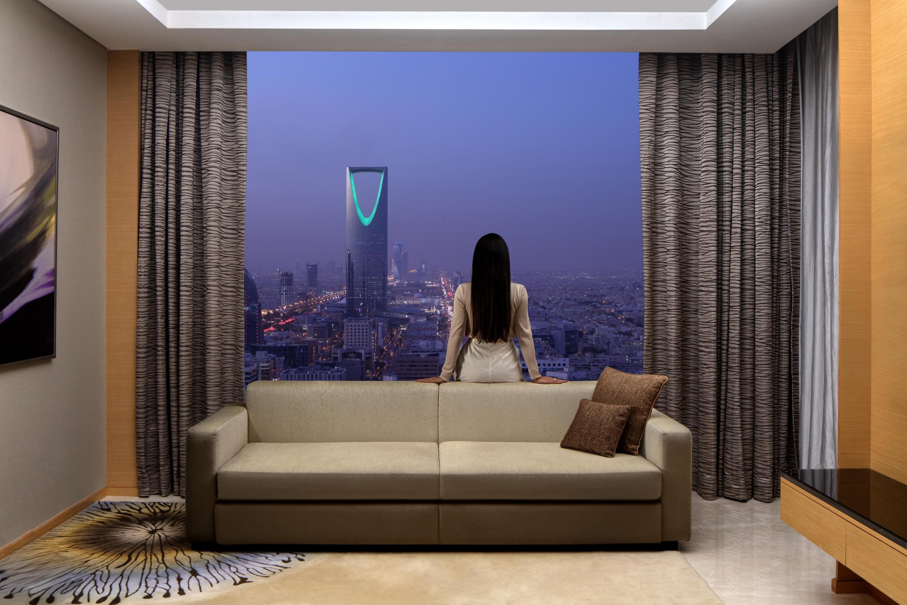 Quarto com uma grande janela, um sofá e vista para a paisagem urbana.