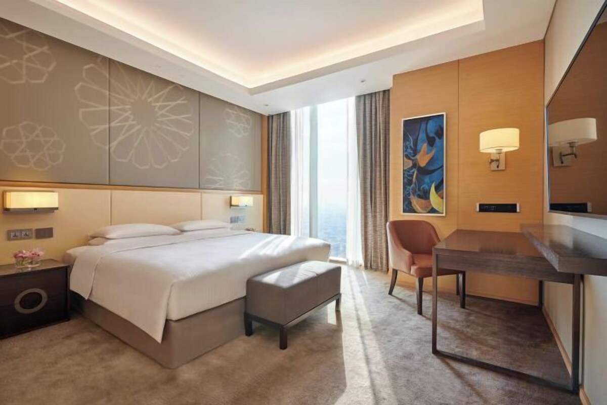 Quarto de hotel com uma cama grande, mesas de cabeceira, escrivaninha e uma cadeira.