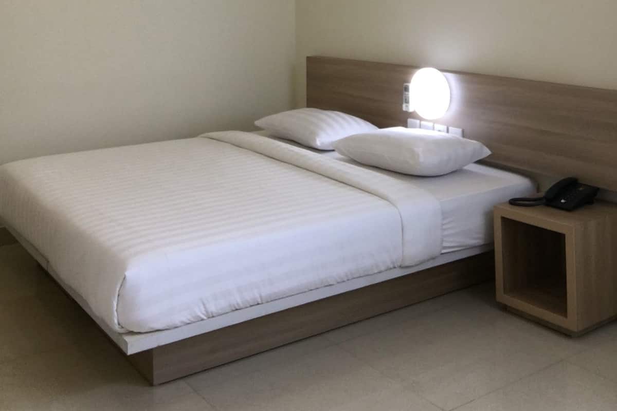 Cama bem arrumada com lençóis e almofadas brancos, mesa de cabeceira com abajur e telefone ao lado direito.