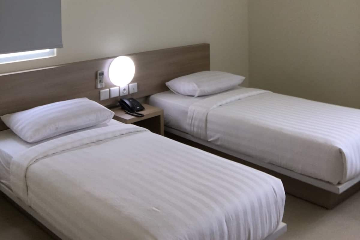 Quarto de hotel com duas camas de solteiro, uma mesa de cabeceira com abajur e um telefone.