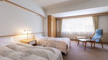 Quarto de hotel com duas camas, uma escrivaninha, uma cadeira e uma janela grande com cortinas.