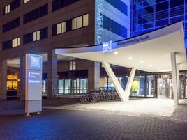 Exterior do hotel ibis budget em Amsterdã Sul, com fachada moderna, entrada destacada com marquise e área de estacionamento para bicicletas.