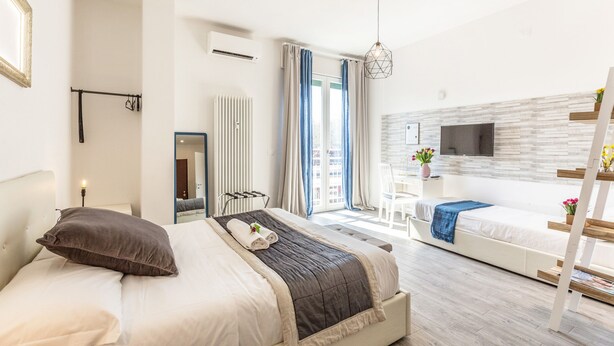 Quarto de hotel moderno com cama, sofá, televisão e varanda com cortinas.