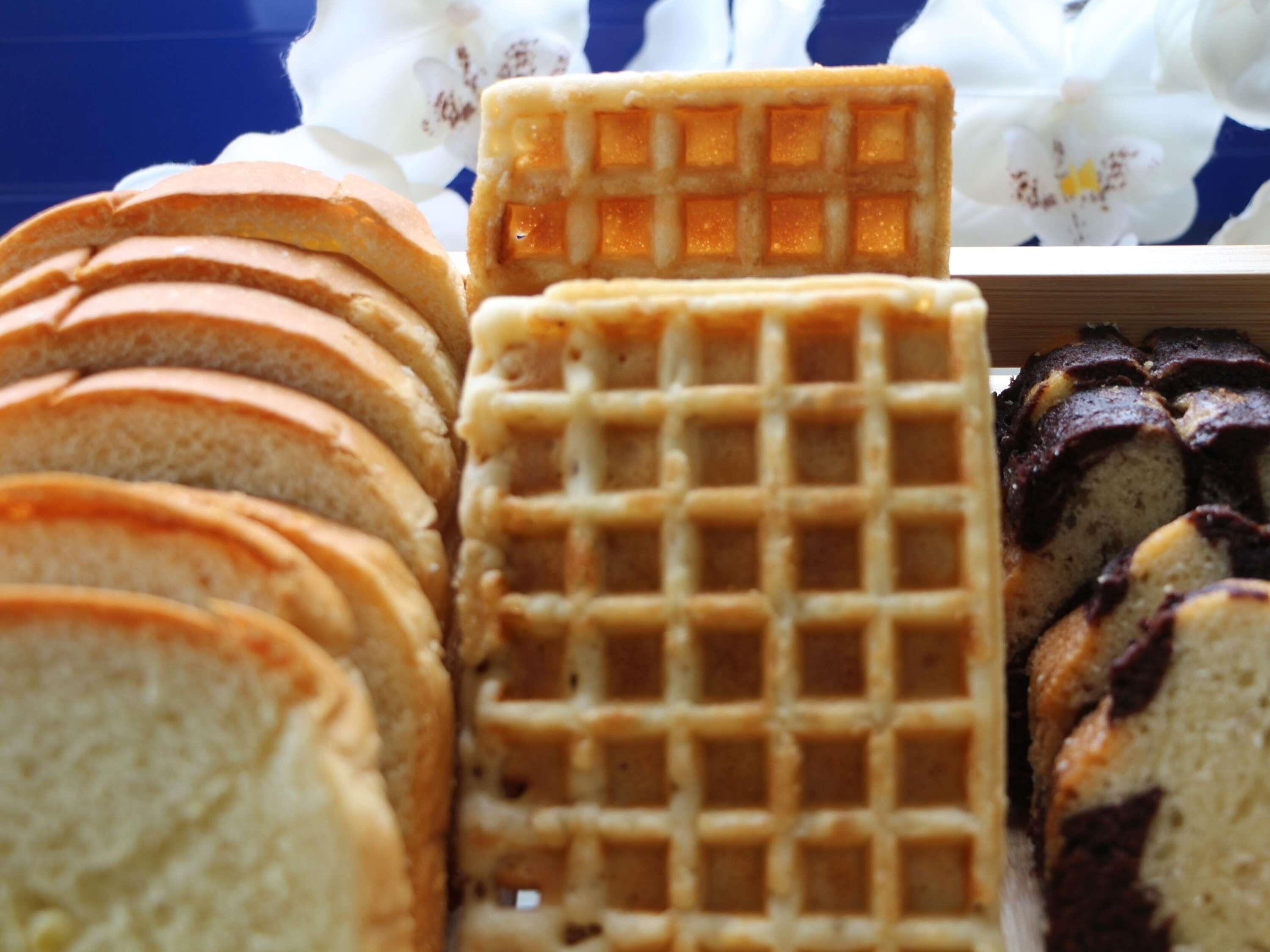 Diversos tipos de pão fatiado e um waffle.