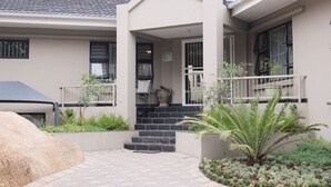 Uma casa moderna com uma escadaria de pedra que leva à porta da frente, rodeada por um jardim com diversas plantas.