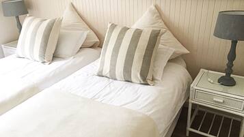 Quarto de hotel com duas camas, cada uma com roupa de cama branca e almofadas listradas. Há duas mesas de cabeceira com abajures.