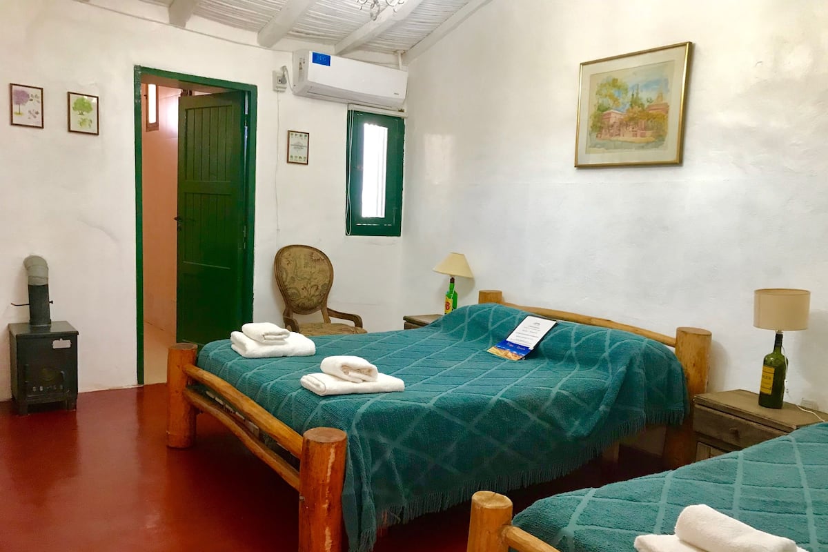 Quarto com cama, cadeira, mesa, abajur e ar-condicionado fixado na parede.