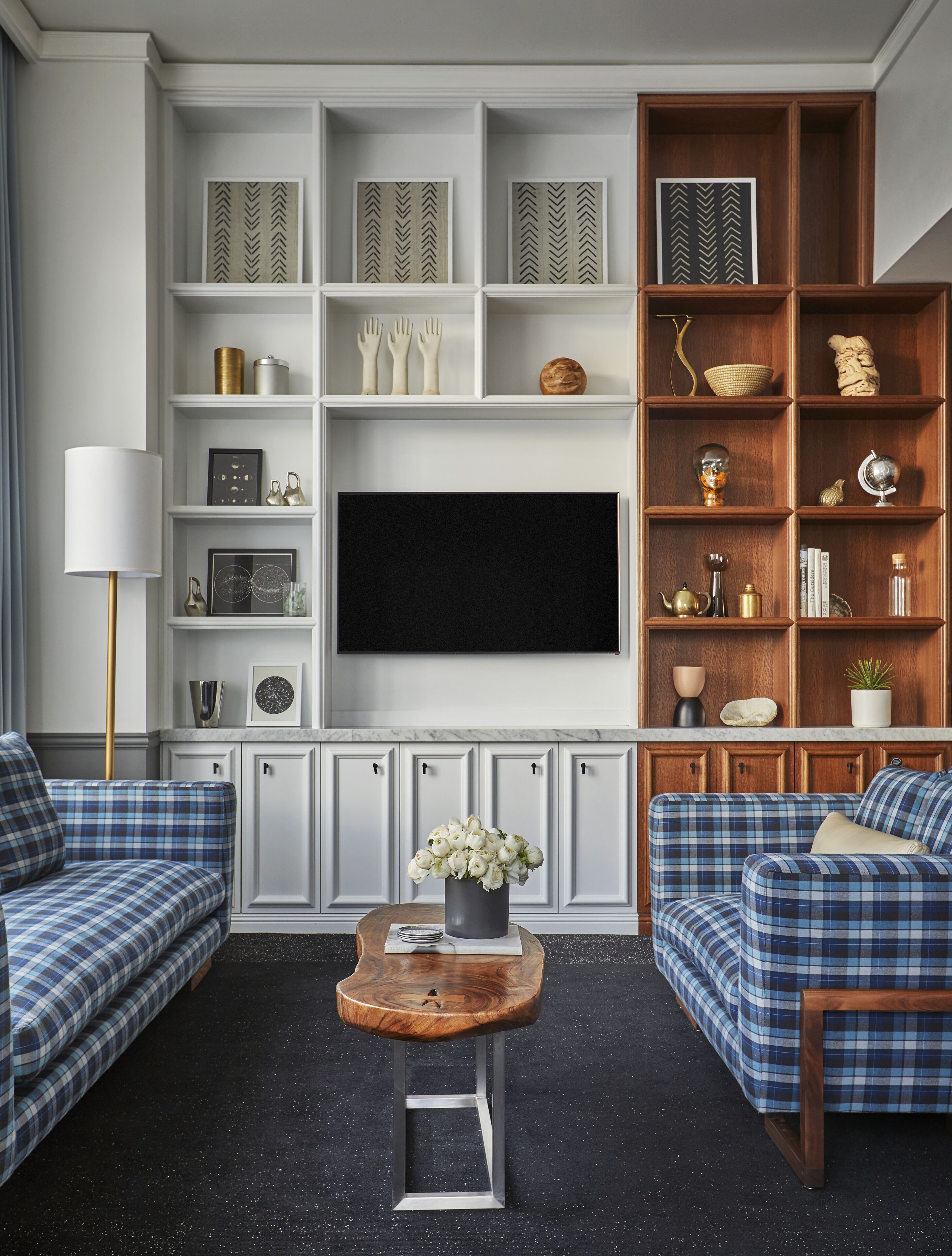 Uma sala de estar moderna com uma televisão de tela grande, dois sofás xadrez, uma mesa de centro e prateleiras embutidas com objetos decorativos.