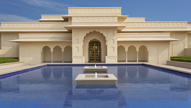 Um edifício grande e ornamentado com uma entrada em arco central e uma piscina na frente.