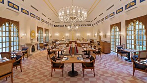 Uma sala de jantar espaçosa com piso xadrez, grandes lustres e decoração de parede elaborada.