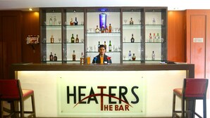 Um bar chamado “HEATERS THE BAR” com prateleiras cheias de garrafas de bebidas e copos, e dois banquetas vermelhas.