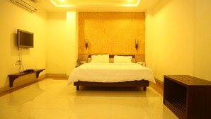 Quarto de hotel com uma cama grande, televisão de tela plana na parede, uma mesinha e ar condicionado fixado na parede.