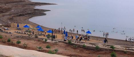 Uma praia com espreguiçadeiras e guarda-sóis, uma área arenosa e mar calmo.